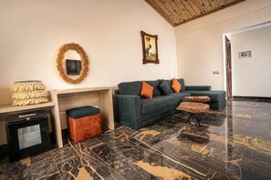 Uma sala de estar moderna com sofá, puf e mesa de centro, lareira e um quadro na parede.