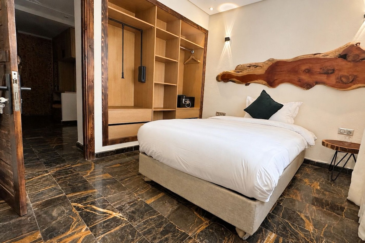 Quarto com cama, guarda-roupa de madeira, luminária fixada na parede e uma cabeceira de madeira singular.