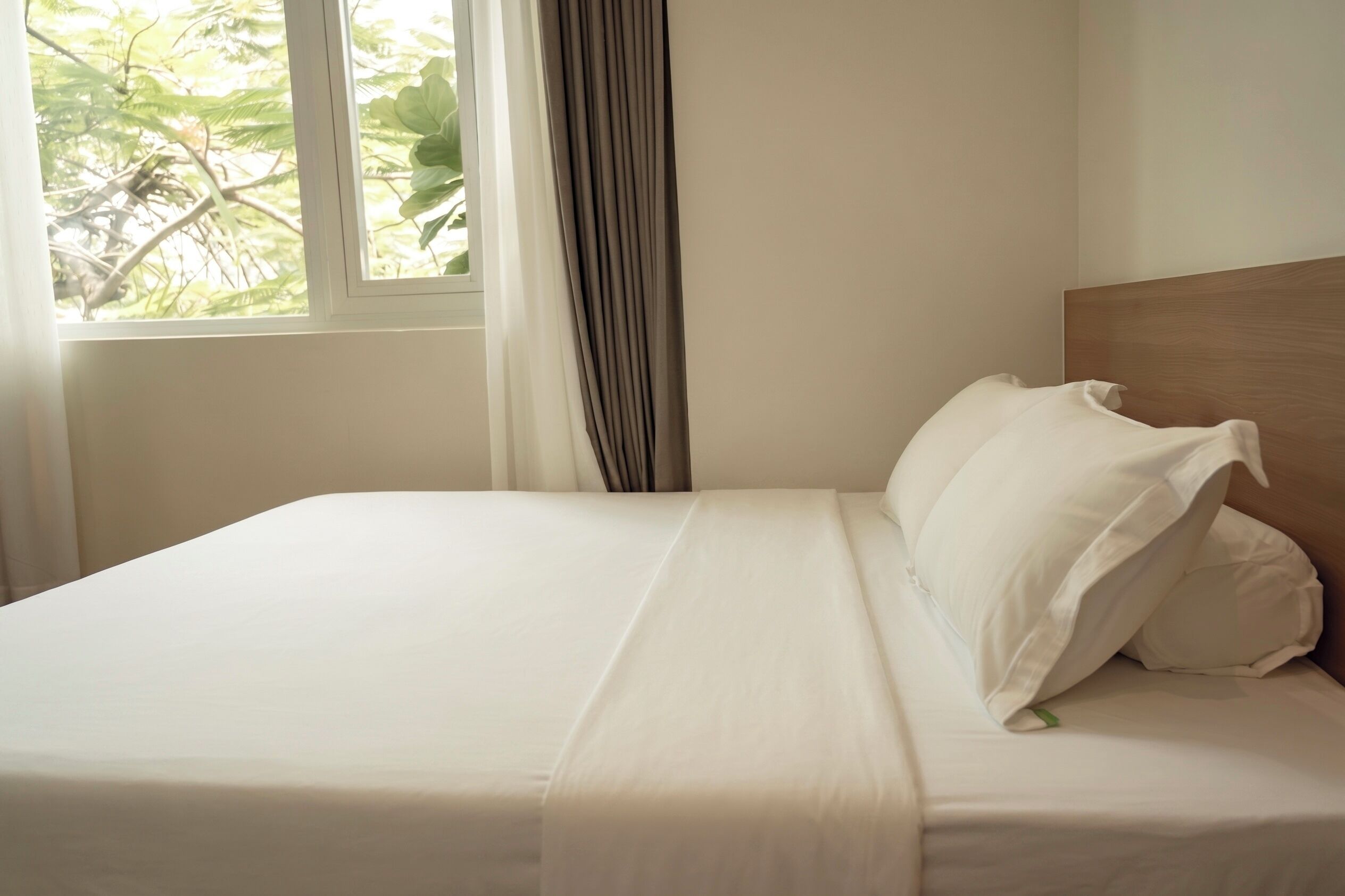 Cama bem arrumada com lençóis brancos em quarto com janela e cortinas.