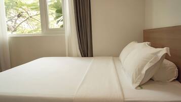 Cama bem arrumada com lençóis brancos em quarto com janela e cortinas.