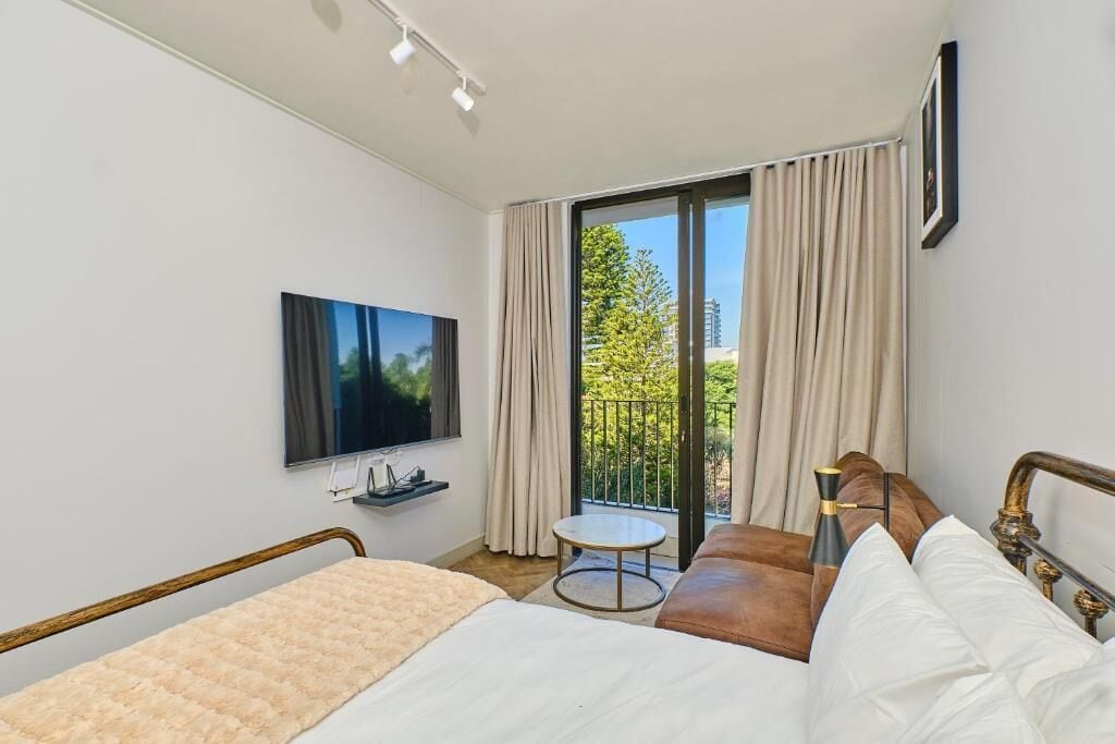 Quarto de hotel com cama, televisão, mesa pequena redonda e varanda com cortinas.