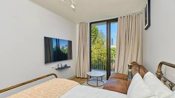 Quarto de hotel com cama, televisão, mesa pequena redonda e varanda com cortinas.