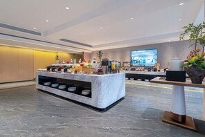 Um lobby de hotel moderno com uma receção de mármore, uma televisão de ecrã plano e uma área de buffet.