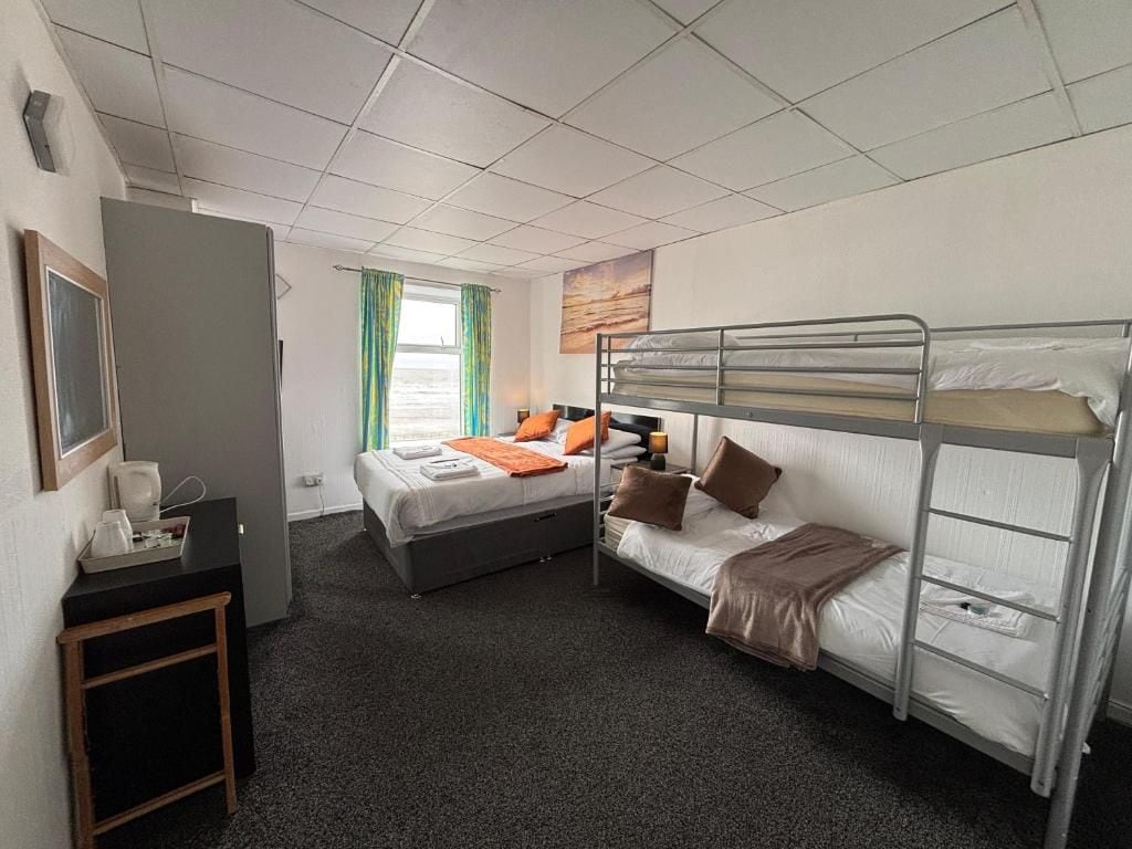 Quarto em dormitório com beliches, uma escrivaninha, uma cadeira e uma janela com cortinas.