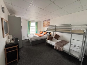 Quarto em dormitório com beliches, uma escrivaninha, uma cadeira e uma janela com cortinas.