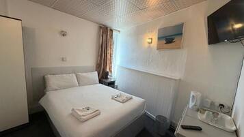 Quarto de hotel com uma cama, mesa de cabeceira com abajur, televisão na parede e um quadro.