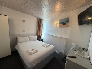 Quarto de hotel com uma cama, mesa de cabeceira com abajur, televisão na parede e um quadro.