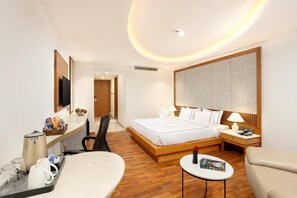 Quarto de hotel com cama, mesa de cabeceira, cadeira e uma mesinha com uma revista.