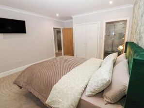 Quarto com cama, televisão na parede, guarda-roupa e banheiro com porta de vidro.