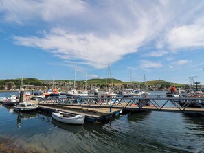 Uma marina com barcos atracados, uma ponte e colinas ao fundo.