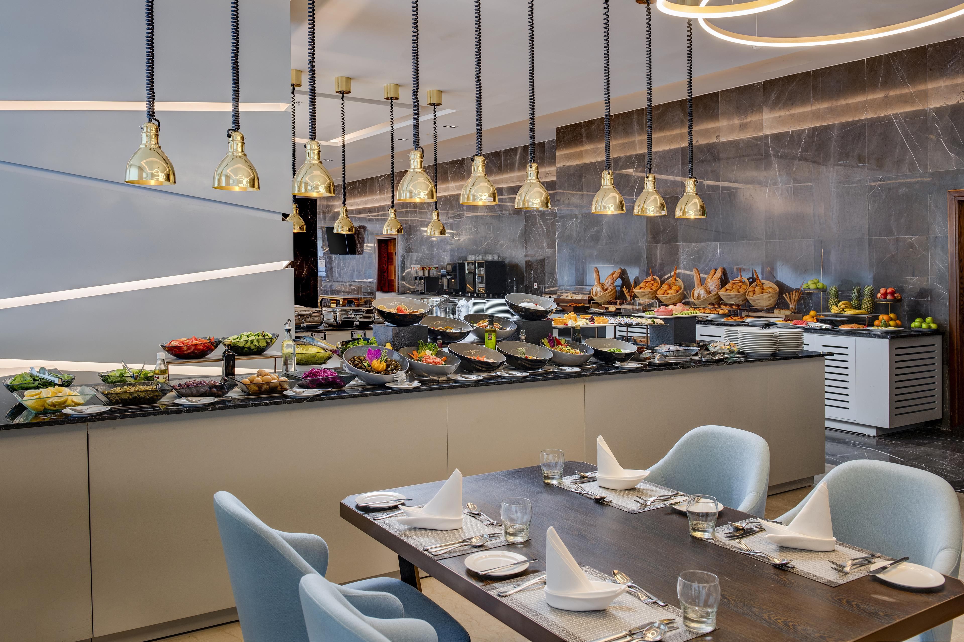 Um restaurante moderno com um balcão extenso, várias luminárias pendentes e uma variedade de opções de comida e bebida.