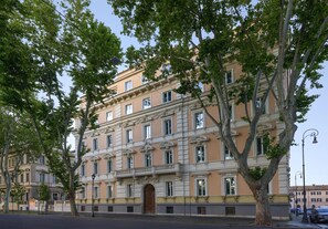 Um edifício de vários andares com arquitetura clássica, destacando uma entrada central com uma porta grande e várias janelas.