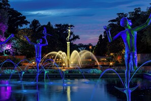 Uma fonte iluminada à noite, com jatos de água e estátuas, em um parque.