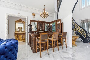 Uma sala imponente com piso de mármore, um candelabro, mobiliário ricamente decorado e uma escadaria com detalhes em preto e dourado.