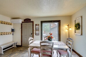 Uma área de refeições com mesa, cadeiras e um banco. Há uma porta com uma placa acima, um ar-condicionado fixado na parede e um luminário também fixado na parede.