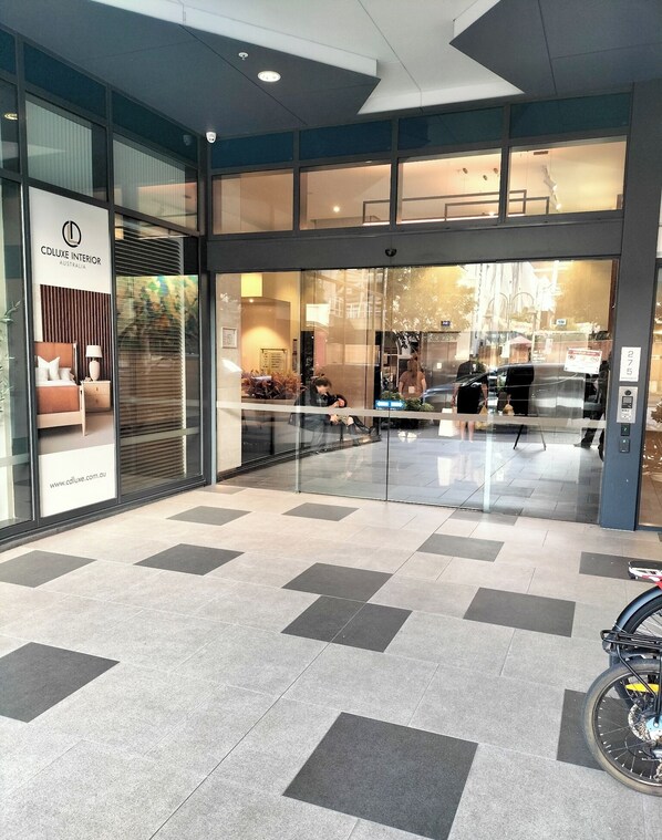 Entrada de um hotel com porta de vidro, uma placa da Cdluxe Interior Australia e piso ladrilhado.