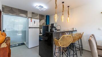 Uma cozinha compacta com geladeira, cafeteira e banquetas.
