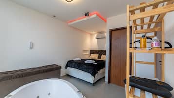 Quarto com cama, prateleira de madeira com artigos de higiene, banheira e ar-condicionado fixado na parede.