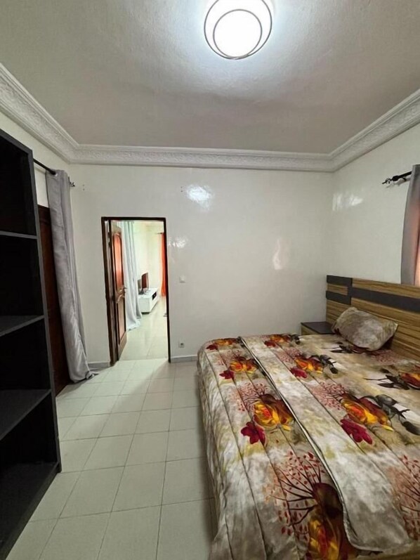 Quarto com cama, cabeceira, mesa de cabeceira, guarda-roupa e porta que dá para outro espaço.