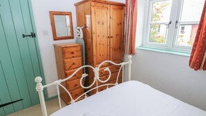 Quarto com cama, guarda-roupa de madeira, penteadeira, espelho e janela com cortinas.