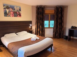 Quarto de hotel com cama, mesa de cabeceira, telefone, janela com cortinas e um quadro na parede.