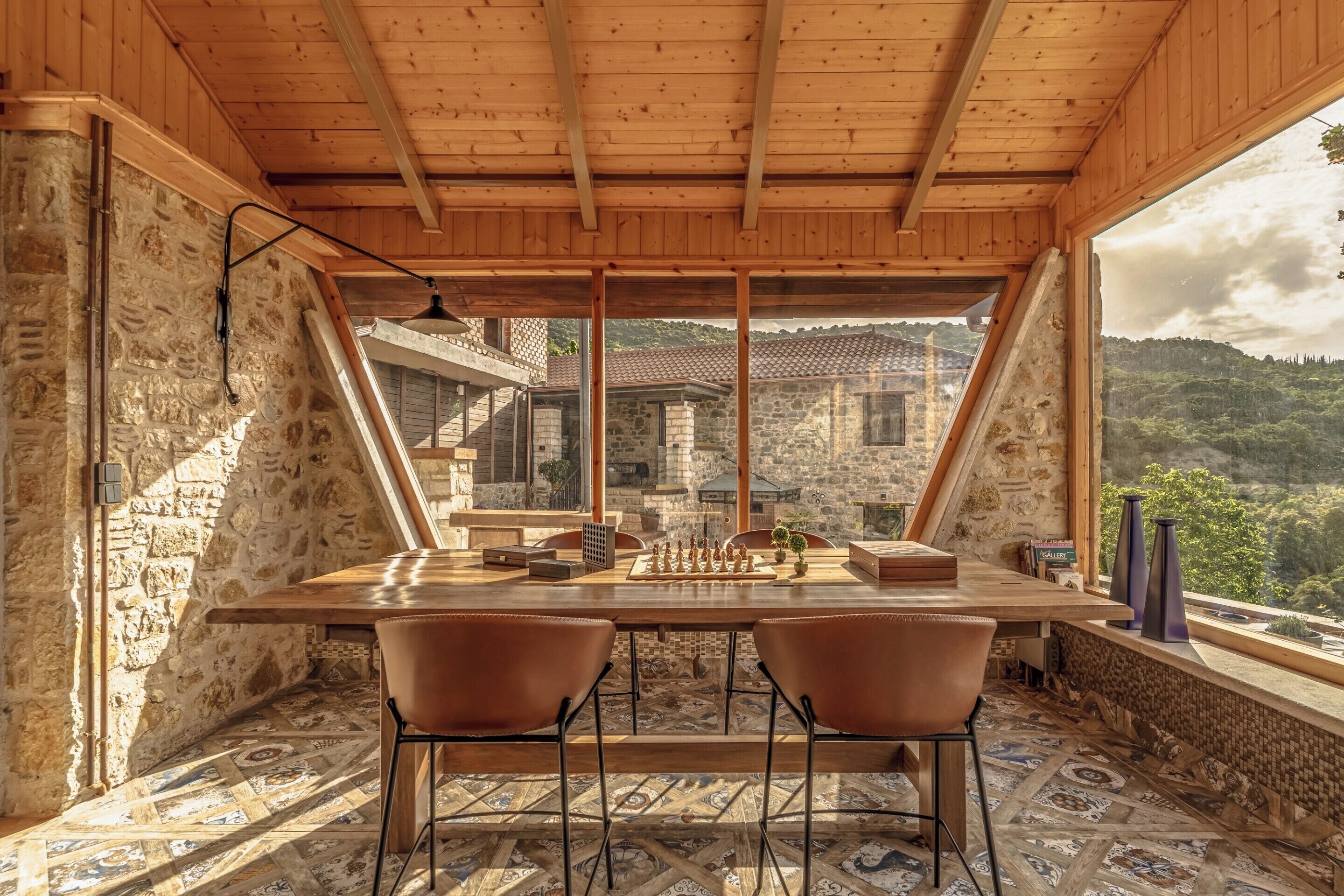 Interior de madeira com um tabuleiro de xadrez, duas cadeiras e vista para um edifício de pedra.
