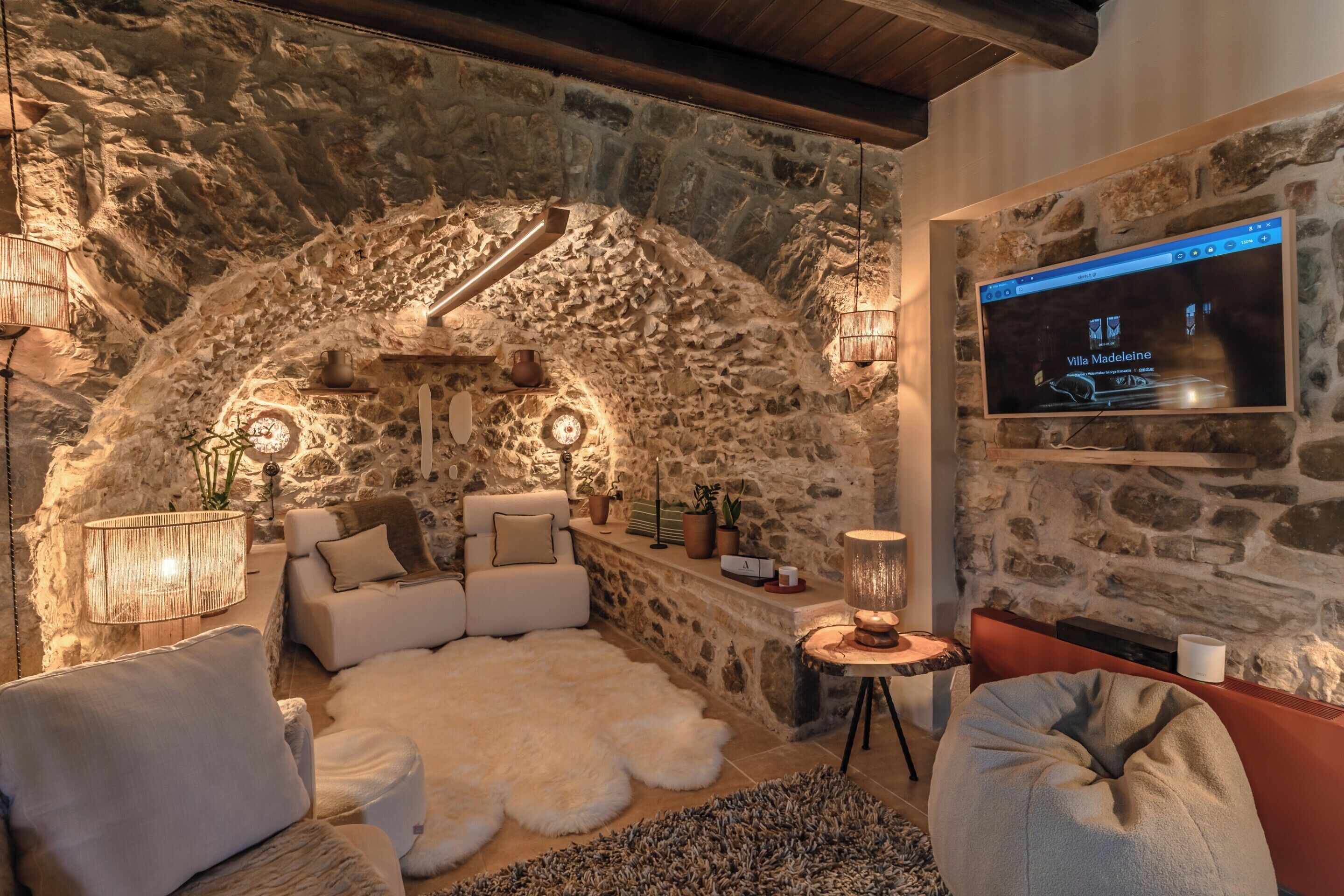 Um quarto acolhedor com paredes de pedra, lareira, sofá e televisão na parede.