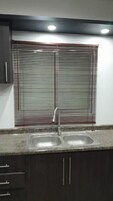 Cozinha com pia dupla, armários escuros e janela com persianas.