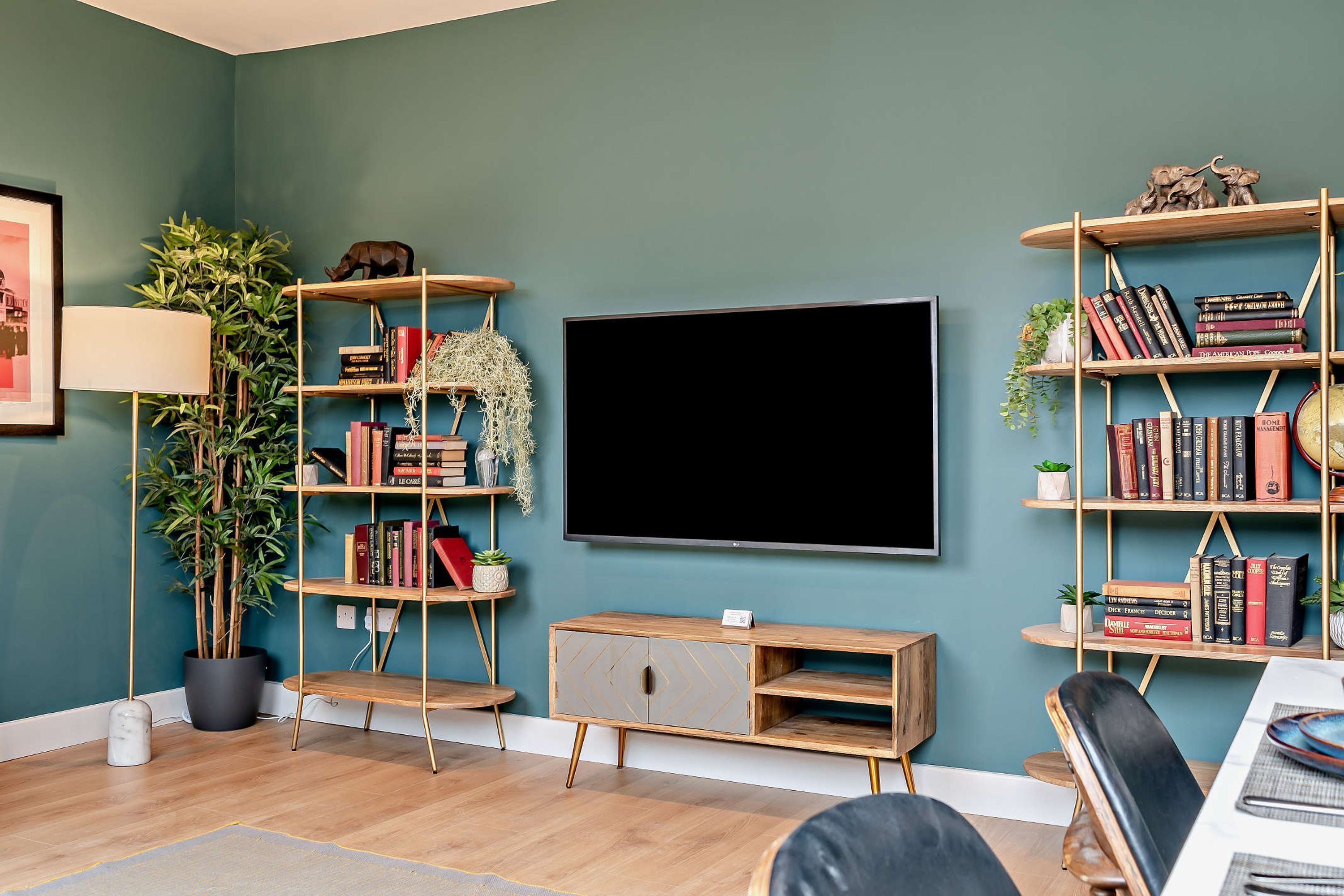 Uma sala de estar com uma grande televisão de tela plana, duas estantes de madeira, um pequeno armário de madeira e um vaso com planta.