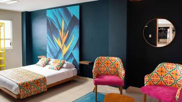 Quarto de hotel com uma cama, duas cadeiras, um grande mural na parede, um espelho e uma janela.