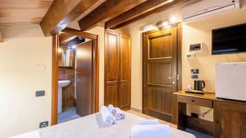 Quarto de hotel com uma cama, uma escrivaninha com chaleira, televisão e portas de madeira.