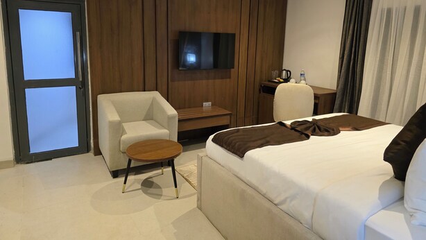 Quarto de hotel com uma cama, sofá, televisão, escrivaninha e uma cadeira.