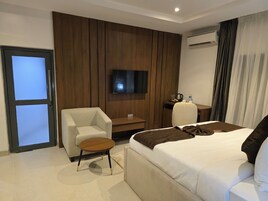 Quarto de hotel com uma cama, sofá, televisão, escrivaninha e uma cadeira.