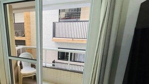 Um interior moderno com porta de vidro deslizante que dá para uma varanda com uma cadeira branca e uma mesa pequena.