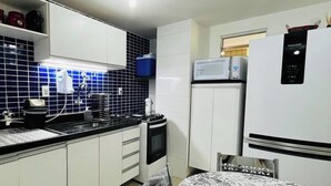 Cozinha compacta com armários brancos, micro-ondas, fogão e pia.