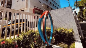 Um edifício com vários andares, entrada para garagem, uma grande escultura de metal e um céu azul límpido.