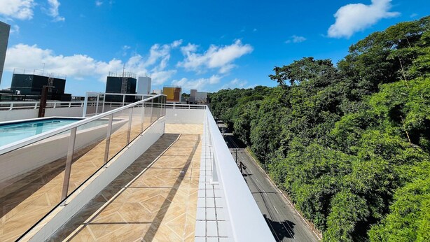 Um terraço no telhado com piscina, guarda-corpos e vista da cidade e vegetação.