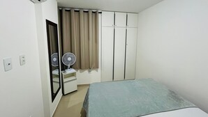 Quarto com cama, guarda-roupa, espelho, ventoinha e luminária de teto.