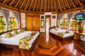 Quarto de hotel com duas camas, piso de madeira, televisão e grandes janelas com cortinas.