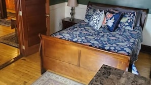 Quarto com cama de madeira, mesa de cabeceira, abajur e tapete.