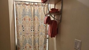 Um banheiro com cortina de chuveiro, porta-toalhas com toalhas, interruptor de luz e porta.