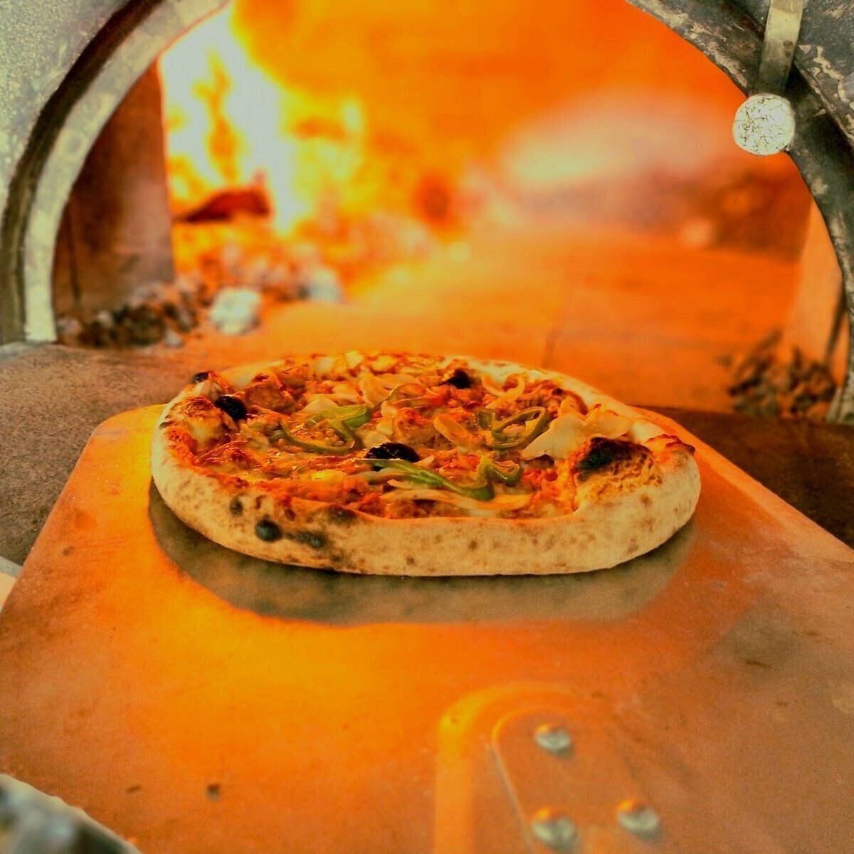 Uma pizza em forno a lenha, com chamas visíveis.