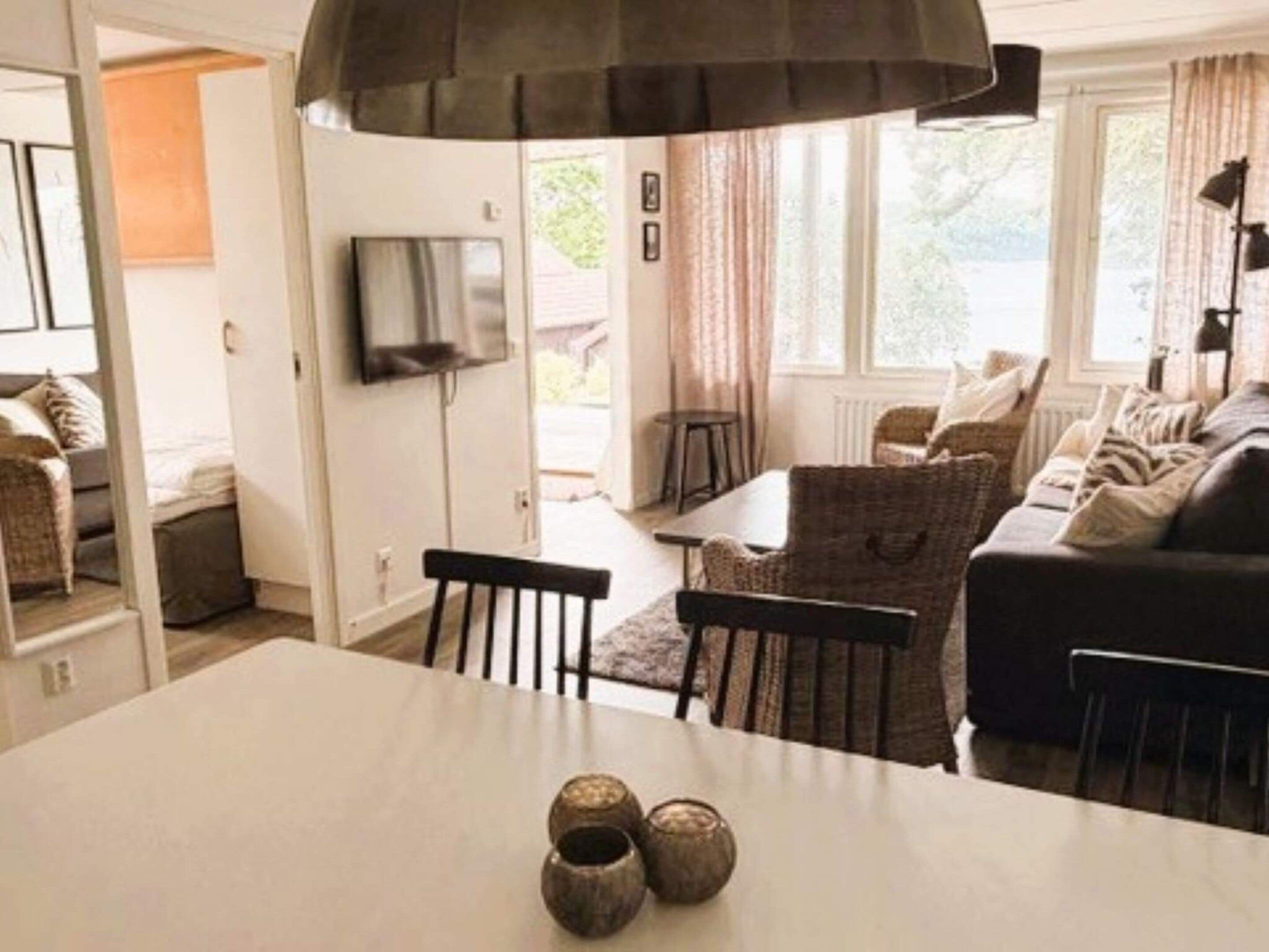Uma sala de estar com sofá, poltronas, mesa e televisão fixada na parede.