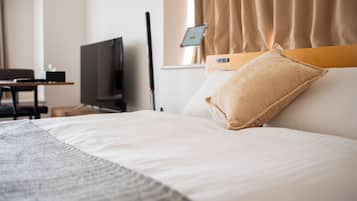 Quarto de hotel com cama, escrivaninha, televisão e janela com cortinas.