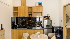 Cozinha compacta equipada com frigorífico, micro-ondas e máquina de lavar roupa. Inclui duas cadeiras e uma pequena mesa com um vaso.
