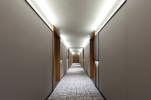 A hotel hallway with a patterned carpet, wooden doors, and a long corridor.