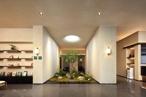 A hotel lobby with a central garden, wooden shelves with books and decorative items, and a reception desk.