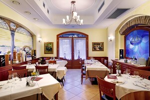 Um restaurante com várias mesas, um lustre e um vitral.