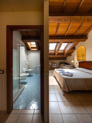 Quarto com cama, mesa de cabeceira, espelho e claraboia.