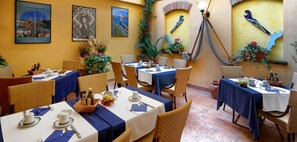 Um restaurante com mesas preparadas para refeições, apresentando uma parede amarela com detalhes decorativos e quadros.